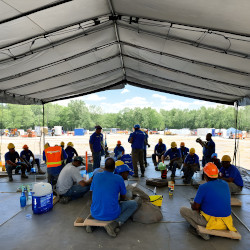 group of workers sitting under a large shade structure.
